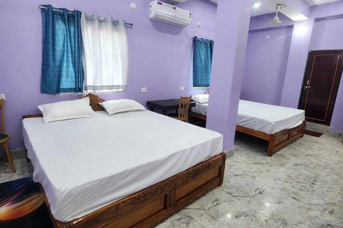 Quarto com duas camas, uma mesa, uma cadeira, ar condicionado e ventoinha no teto.