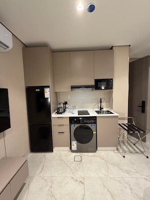 Uma cozinha compacta com lava-louças embutida, micro-ondas e geladeira preta.