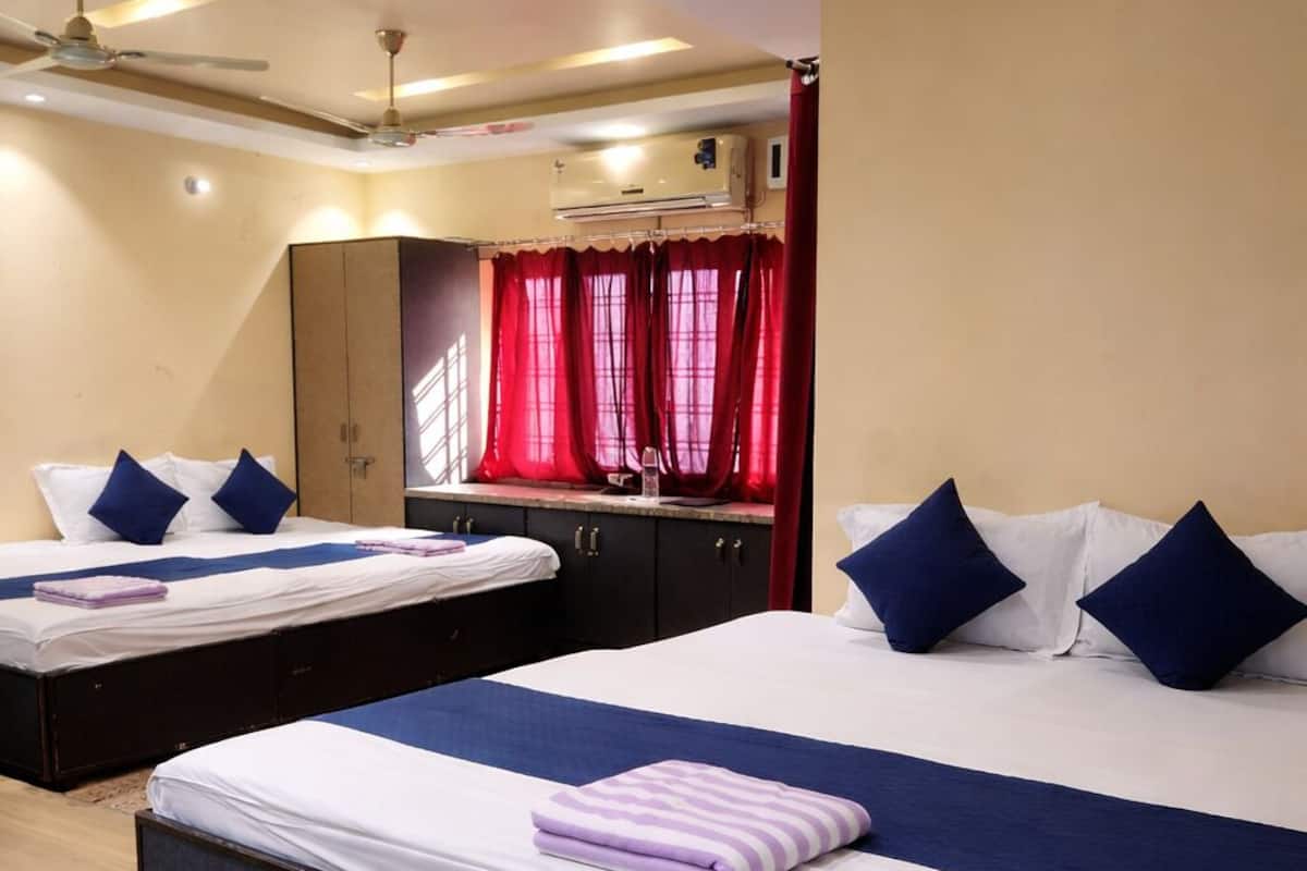 Quarto de hotel com duas camas, um guarda-roupa, um ventilador de teto e uma janela com cortinas vermelhas.