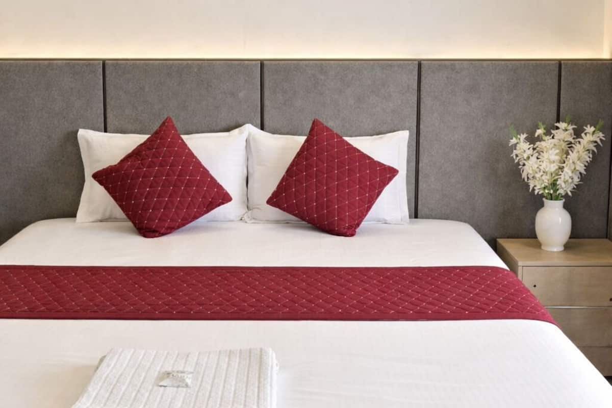 Uma cama bem arrumada com um edredom branco e vermelho, duas almofadas vermelhas e uma toalha branca dobrada sobre a cama.