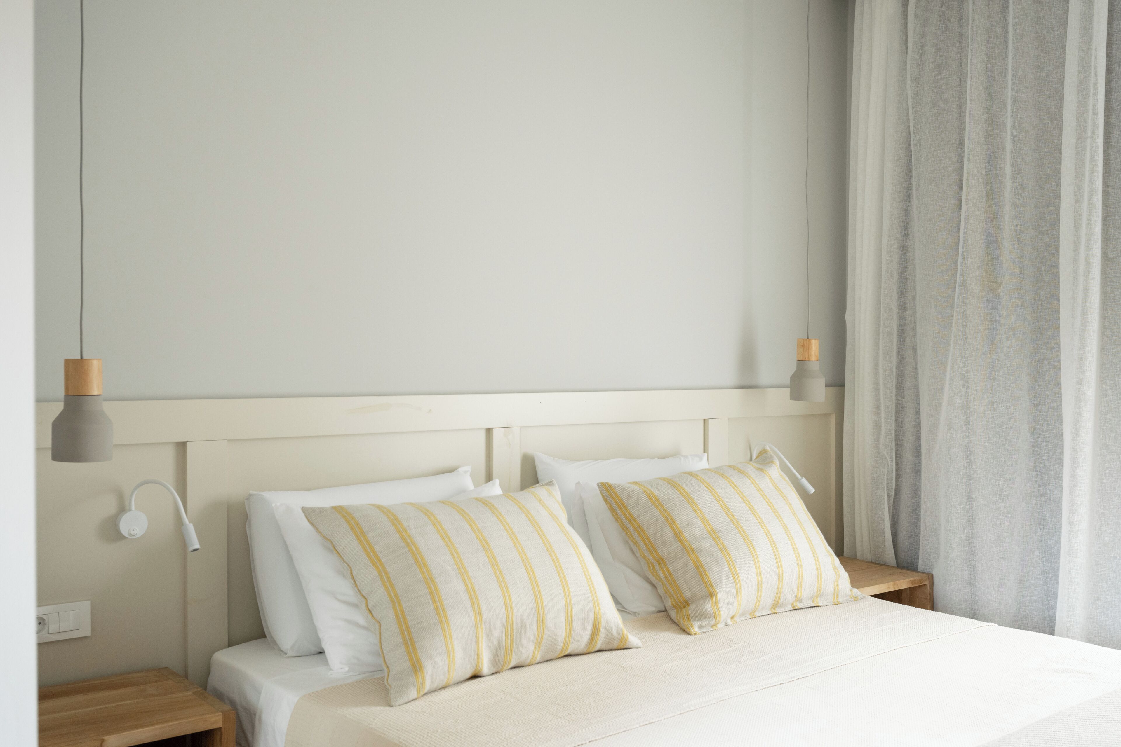 Quarto com cama, duas mesas de cabeceira, um criado-mudo, luminária na parede e cortina.