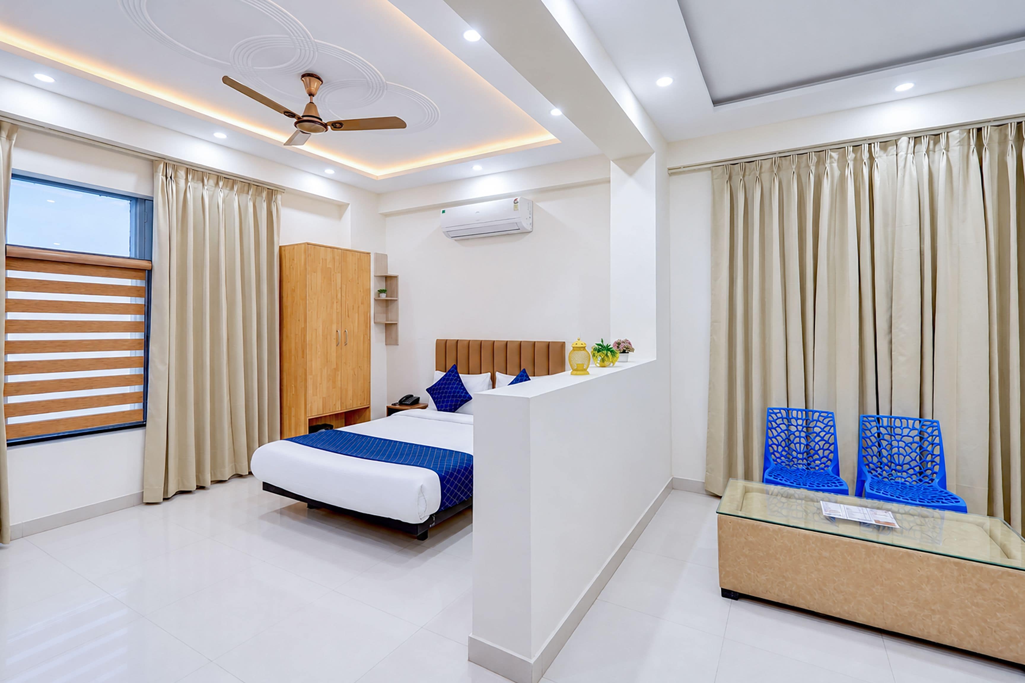 Quarto de hotel moderno com cama, escrivaninha, guarda-roupa e ventoinha no teto.