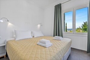 Quarto de hotel com uma cama, duas mesas de cabeceira, uma janela com cortinas e vista para áreas verdes.