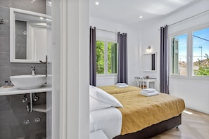Quarto de hotel moderno com uma cama grande, banheiro com pia e janela com cortinas.