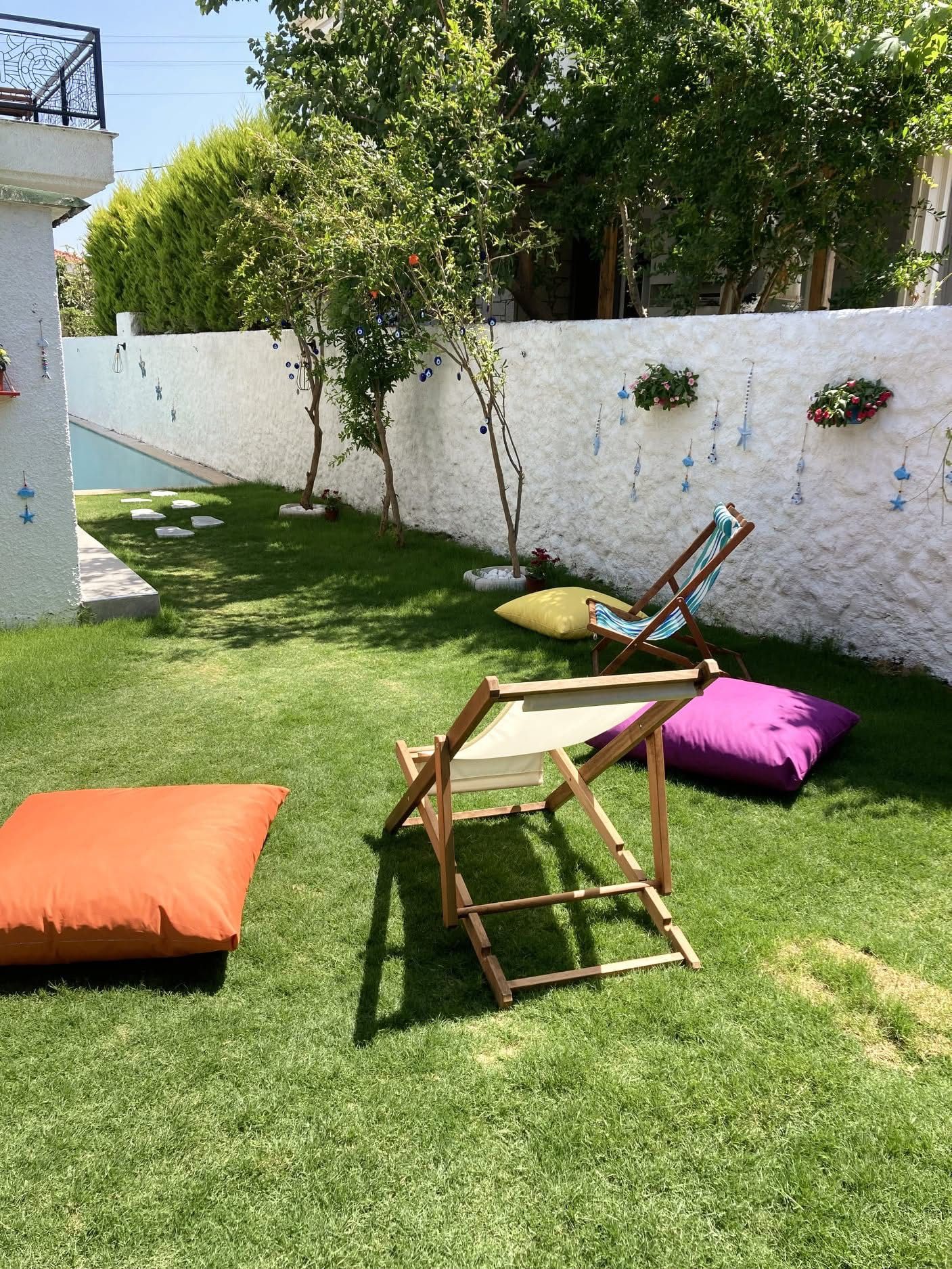 Um quintal com uma cadeira de madeira no deck, uma piscina pequena e uma parede branca com detalhes decorativos.