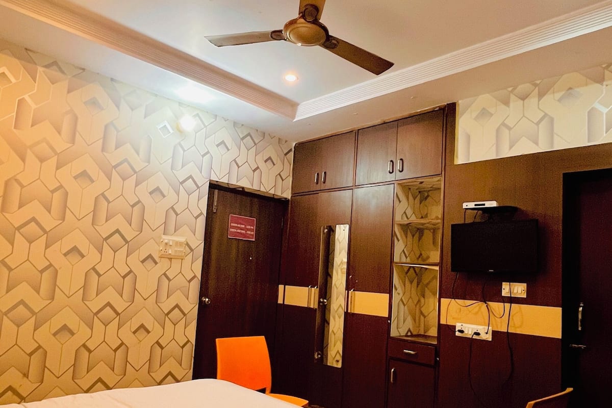 Quarto de hotel com cama, ventoinha no teto, guarda-roupa, televisão e parede estampada.