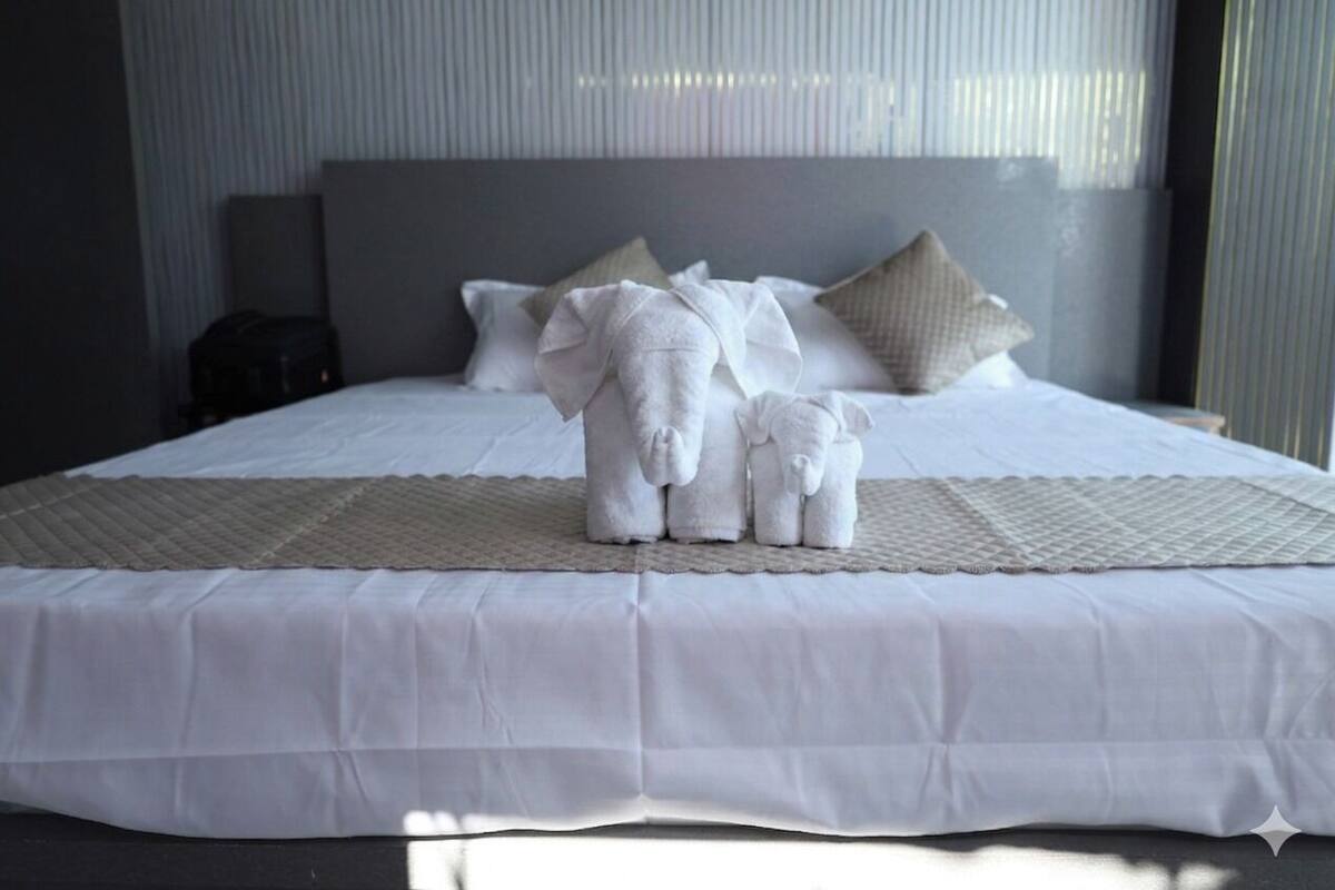 Cama bem arrumada com edredom branco e arranjo decorativo de toalhas.