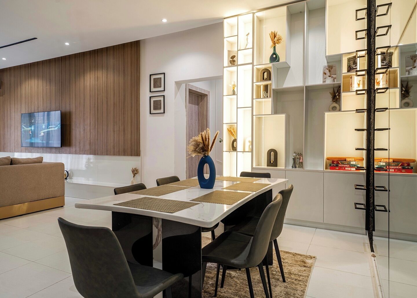 Uma sala de estar moderna com sofá, televisão, área de jantar com mesa e cadeiras, e cozinha com prateleiras abertas.