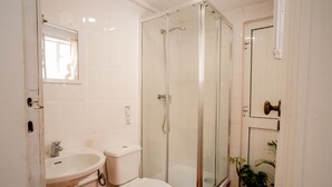Casa de banho com cabine de duche em vidro, lavatório e sanita.