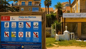 Placa com informações sobre proteção da praia, um edifício residencial e um terraço de bar.