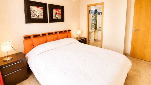 Quarto com cama, mesa de cabeceira, abajur, quadro e porta.