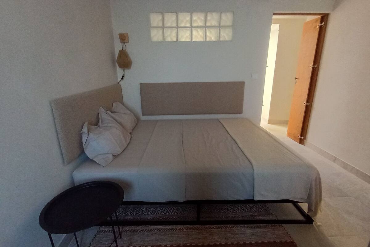 Quarto com uma cama, uma cadeira, uma janela e uma porta.