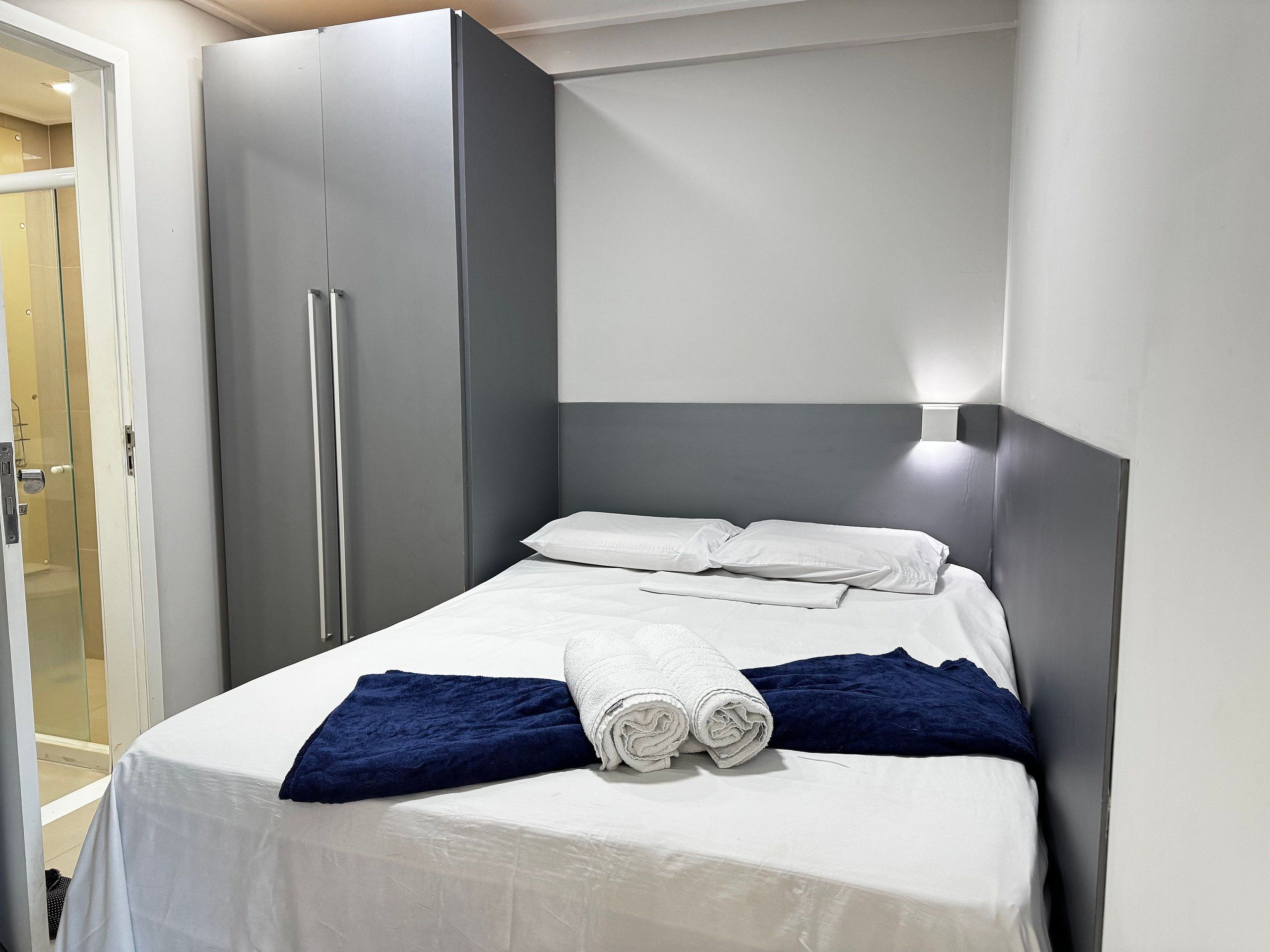Quarto de hotel com cama, guarda-roupa e banheiro visível através de uma porta aberta.