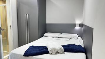 Quarto de hotel com cama, guarda-roupa e banheiro visível através de uma porta aberta.