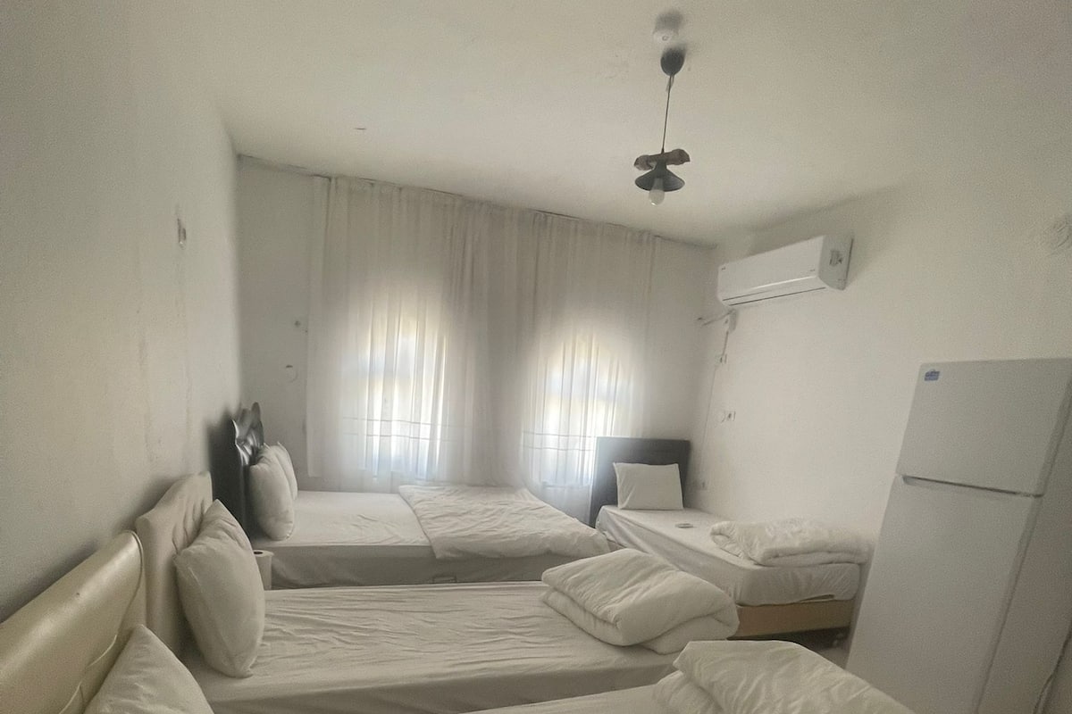 Quarto com três camas, ventilador de teto, ar condicionado e geladeira.