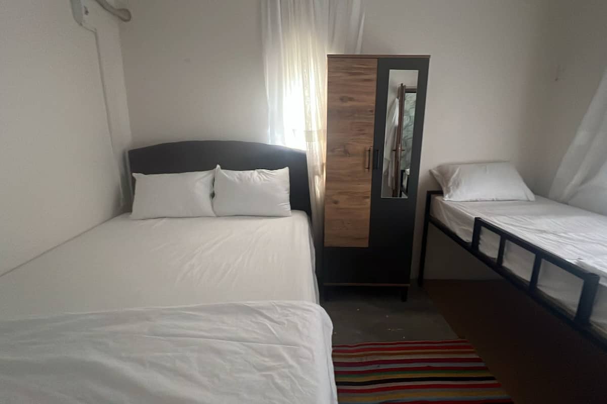 Quarto pequeno e limpo com duas camas de solteiro, um guarda-roupa de madeira e um tapete listrado.