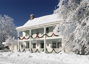 Um edifício coberto de neve com varanda, colunas e uma placa que diz 'Deerfield Inn'.