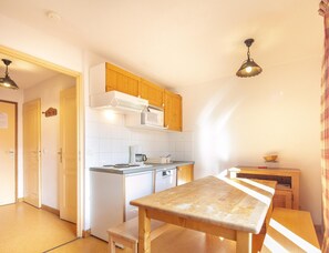 Uma cozinha compacta com armários brancos, micro-ondas, cafeteira e uma mesa de madeira.