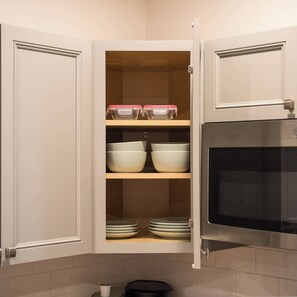Uma cozinha com armários, micro-ondas e prateleiras para guardar utensílios.