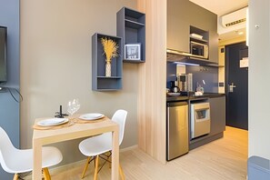 Uma cozinha moderna com eletrodomésticos embutidos, um espaço de refeições com mesa e cadeiras, e uma prateleira fixada na parede com objetos decorativos.