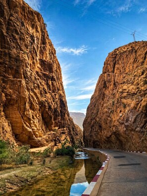 Uma estrada estreita em um cânion, com um canal de água visível à esquerda e paredões rochosos em ambos os lados.