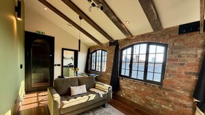 Uma sala de estar moderna com um sofá, uma janela ampla com vista, paredes de tijolos aparentes e teto com vigas de madeira.