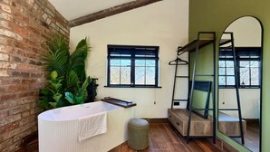 Casa de banho com banheira, janela, espelho e parede de tijolos.