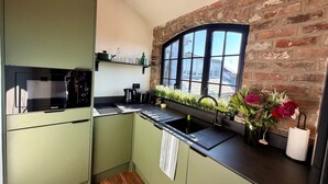 Cozinha com armários verdes, bancada preta, janela com vista e parede de tijolos.