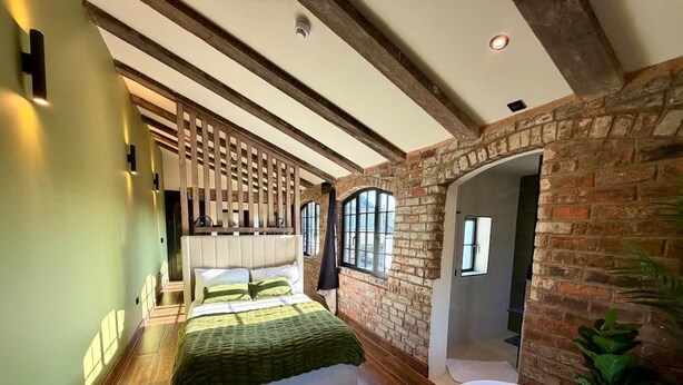Quarto com cama, vigas de madeira, paredes de tijolo e uma janela.