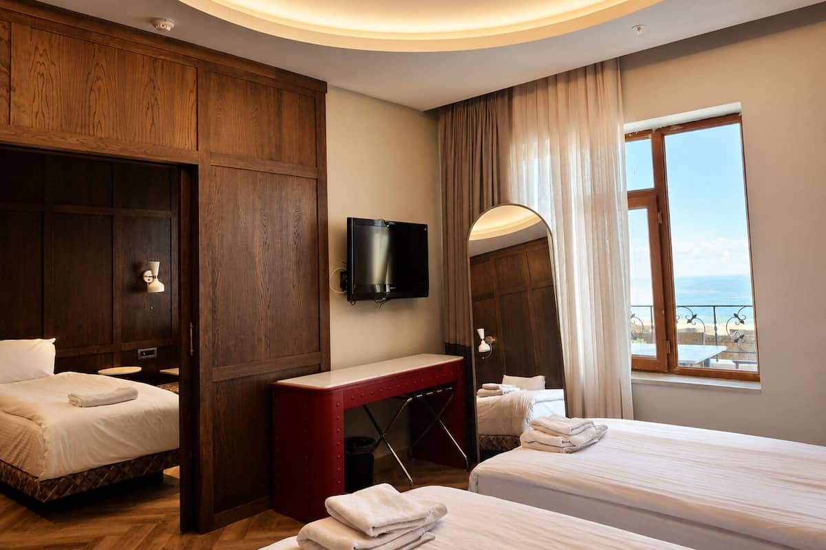 Quarto de hotel com guarda-roupa de madeira, uma secretária, televisão e cama com toalhas.