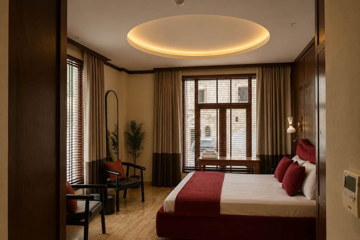 Quarto de hotel com uma cama grande, uma escrivaninha, uma cadeira, um vaso de plantas e uma janela com cortinas.