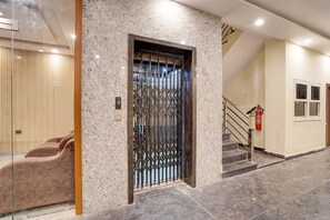 Um hall com parede de mármore, portão de metal, escada e extintor de incêndio.