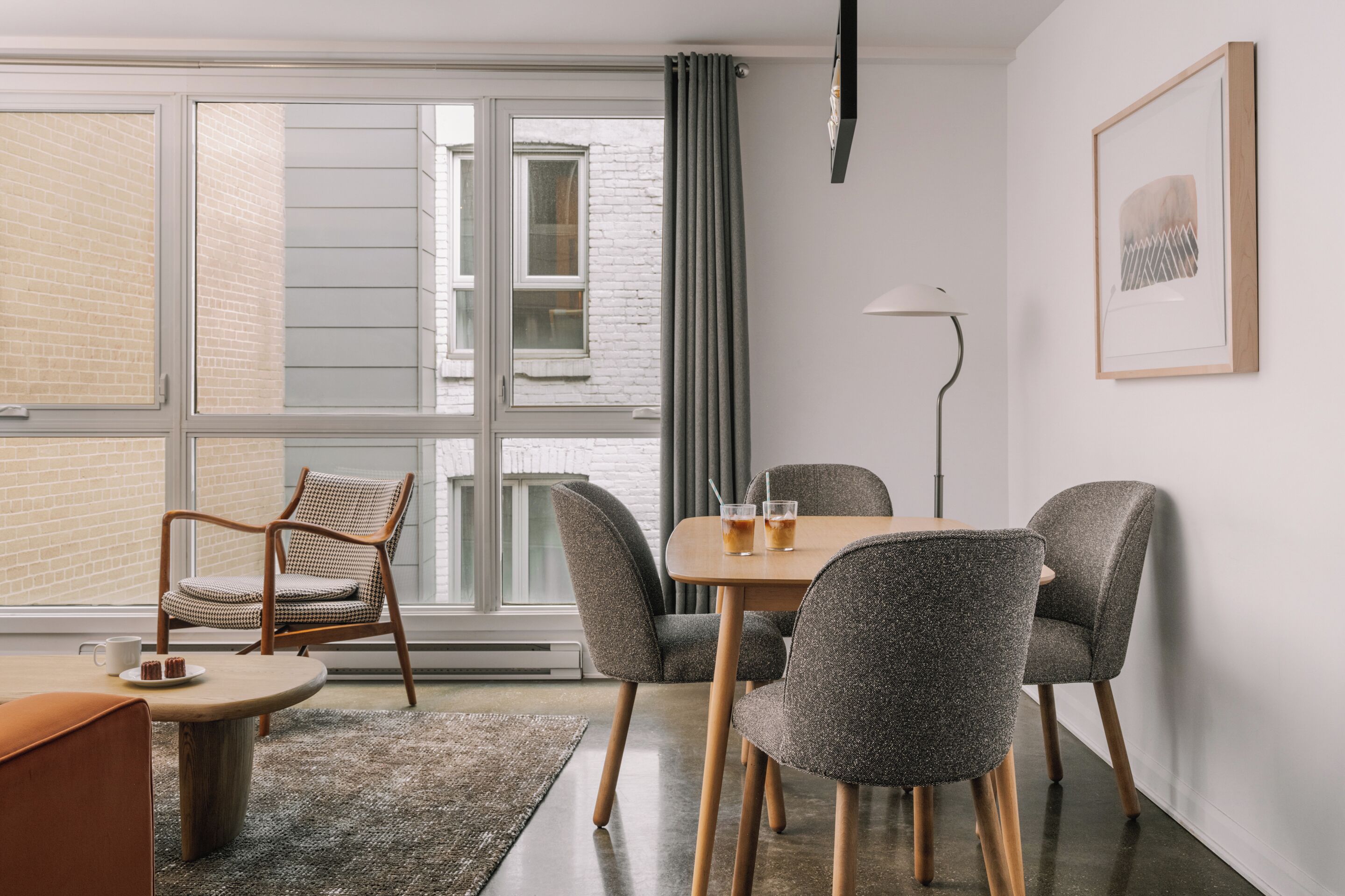 Uma área de refeições moderna com uma mesa, cadeiras e vista para um edifício de tijolos através de grandes janelas.
