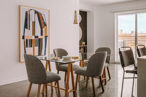 Uma área de refeições moderna com mesa de vidro, cadeiras estofadas cinzas e um grande quadro abstrato na parede.