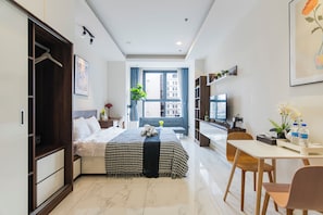 Quarto de hotel moderno com cama, escrivaninha, cadeira, guarda-roupa, televisão e janela com vista para edifícios.