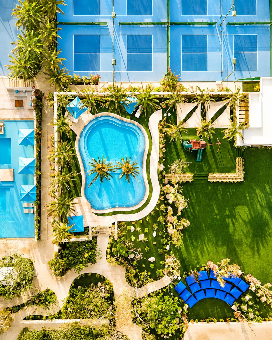 Vista aérea de um resort com piscina central, palmeiras e quadra de tênis.