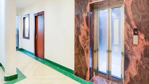 Um corredor com duas portas, uma parede de mármore e um elevador.