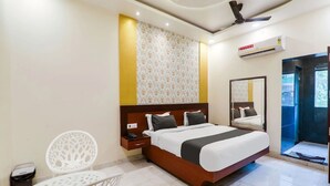 Quarto de hotel com cama, uma mesinha, duas cadeiras, ventoinha no teto, aparelho de ar condicionado e um espelho grande.
