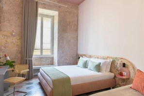 Quarto com cama, cadeira, escrivaninha, janela com cortinas e prateleira na parede.