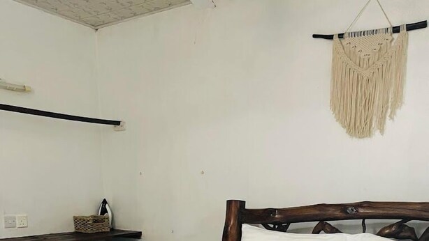 Cama bem arrumada com roupa de cama branca, colcha estampada e um pendente de macramé na parede.