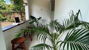 Uma pequena varanda fechada com chão de azulejos, um banquinho de madeira, um vaso de planta e um laptop no peitoril da janela.