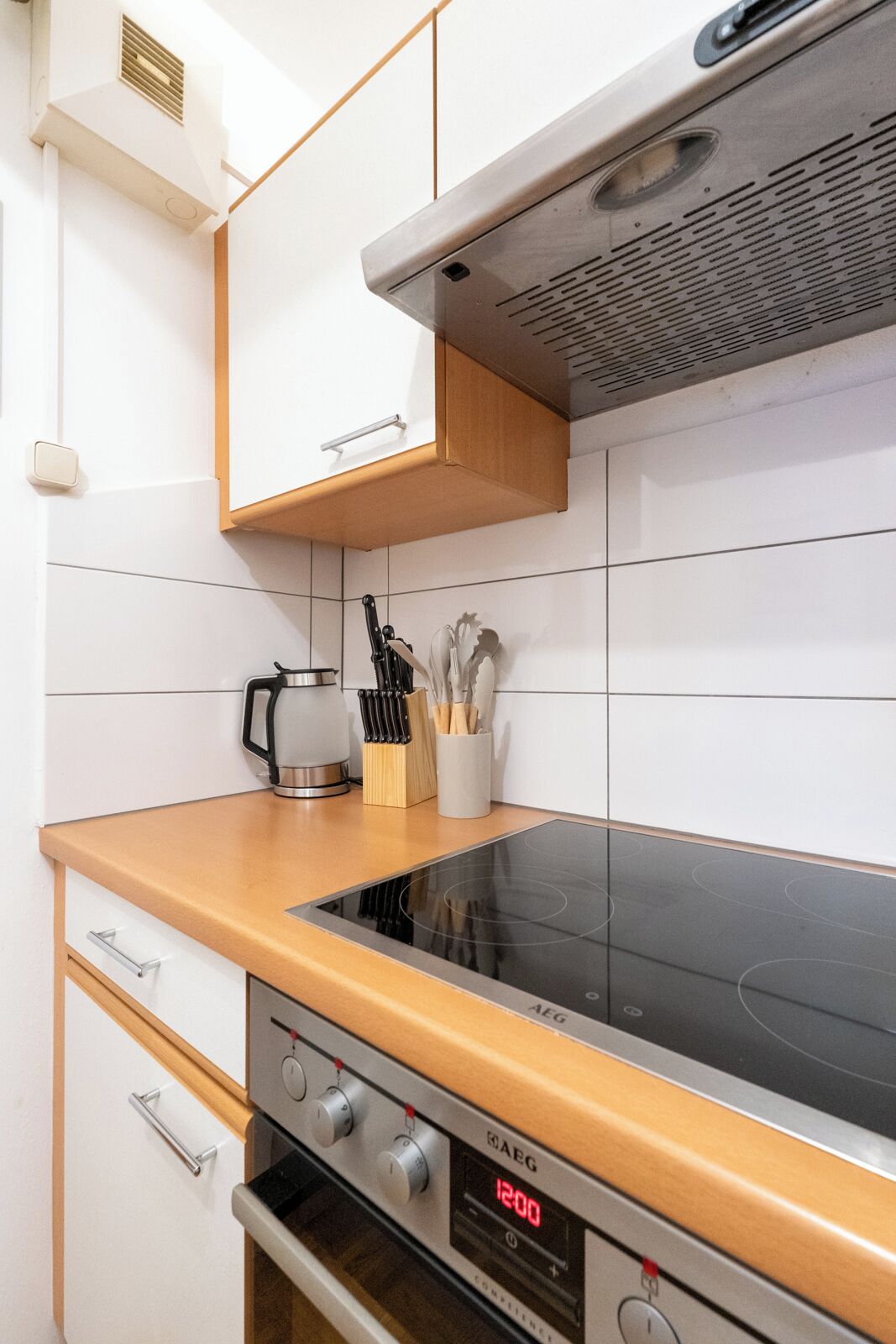 Cozinha com fogão por indução preto, relógio digital e máquina de café.