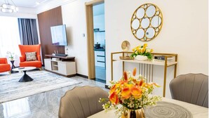 Uma sala moderna com televisão, poltrona laranja e área de jantar com um vaso de flores.