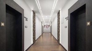 Um corredor comprido e estreito, com paredes escuras e soalho de madeira, que leva a uma série de portas em ambos os lados.