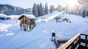 Estância de esqui coberta de neve, com um chalé de madeira, teleféricos e céu limpo.