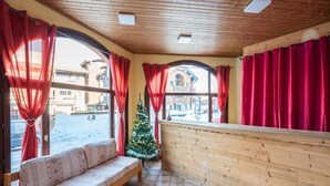 Um quarto acolhedor com um banco de madeira, um pinheiro de Natal e grandes janelas com cortinas vermelhas.