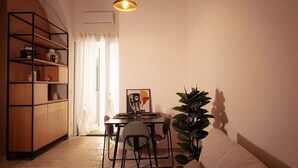 Uma área de refeições com mesa, cadeiras, estante e planta em vaso.