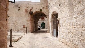 Um corredor de pedra arqueado com um carro branco estacionado no final, que leva a um edifício com uma porta verde.
