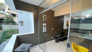 Interior moderno com divisória de vidro, uma pequena varanda e uma cadeira amarela.