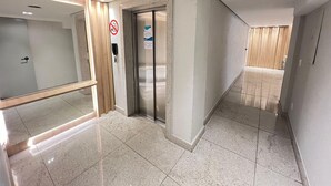 Corredor de hotel com elevador de vidro, placa de proibido fumar e um espelho refletindo o interior.